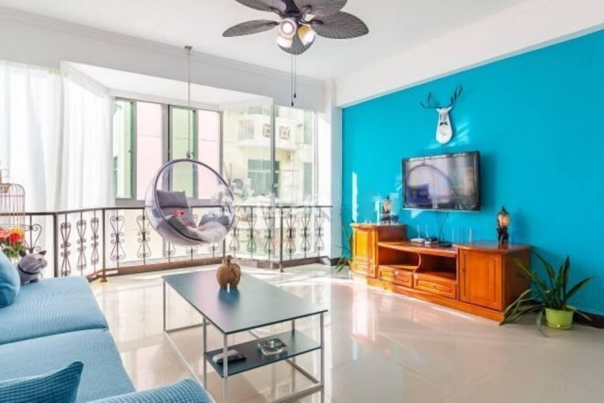 Sala de estar com sofá, mesa de centro, televisão e varanda com cadeira suspensa.