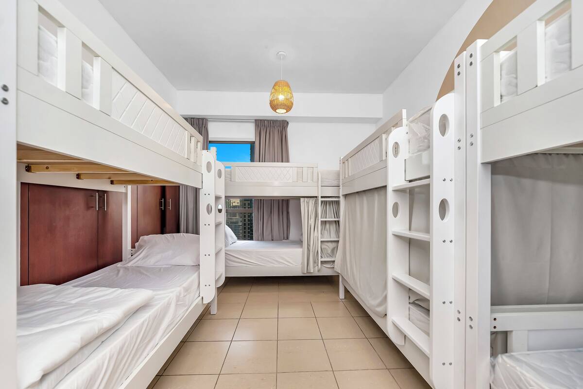 Um quarto com beliches, uma janela com cortinas e um lustre.