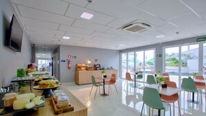 Um café moderno com balcão de madeira, cadeiras verdes e laranja, e vista para o exterior através de grandes janelas.