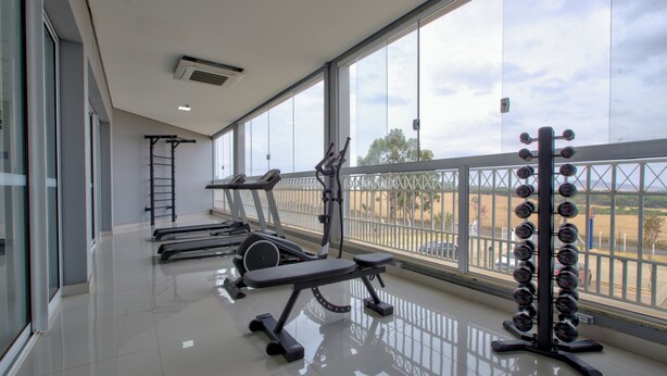 Academia com equipamentos de ginástica, amplas janelas e vista para o exterior.