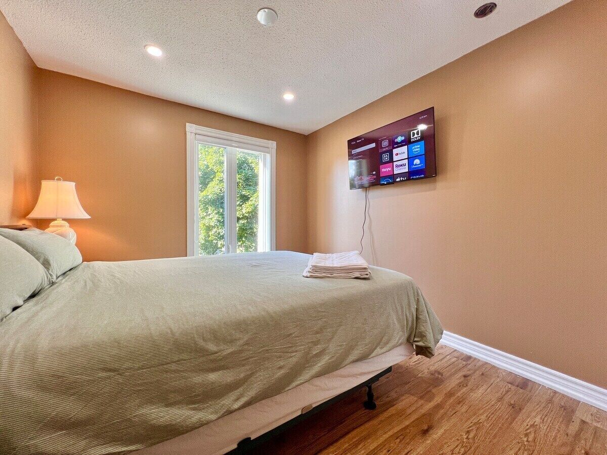 Um quarto com cama, televisão fixada na parede, janela e porta.