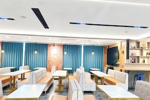 Interior moderno de restaurante, com cabines e mesas, cortinas azuis, parede de tijolos e área de bar.