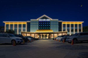 Hotel com um amplo estacionamento e diversos carros estacionados na frente.