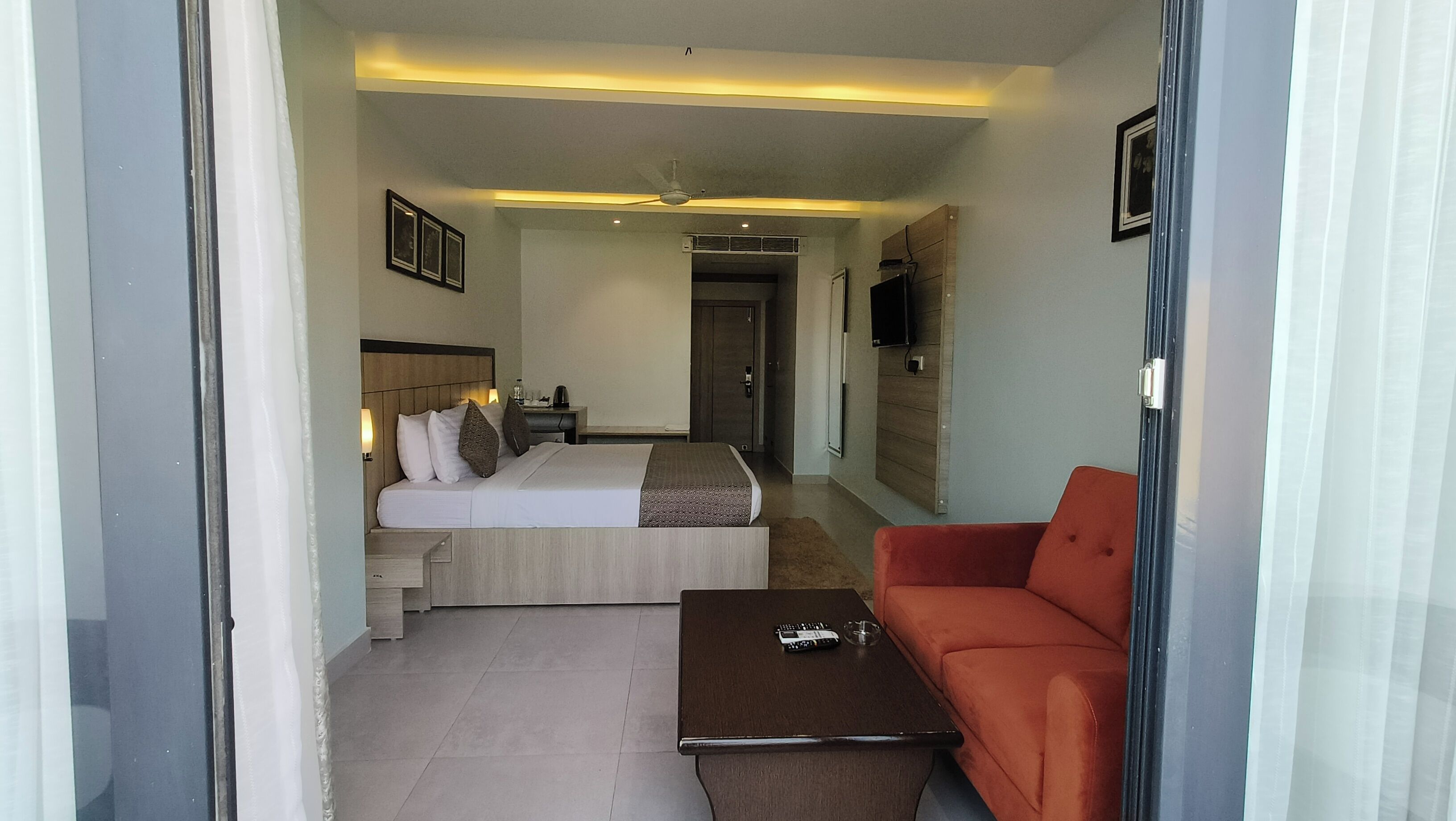 Quarto de hotel com cama, sofá, mesa de centro e televisão.