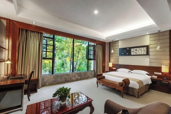 Quarto de hotel com uma janela grande, uma cama, uma escrivaninha, uma cadeira e uma mesa de cabeceira.