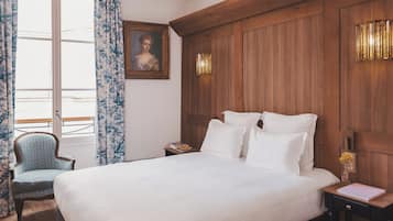 Quarto com uma cama grande, cabeceira de madeira, mesa de cabeceira com abajur, uma cadeira e uma janela com cortinas.
