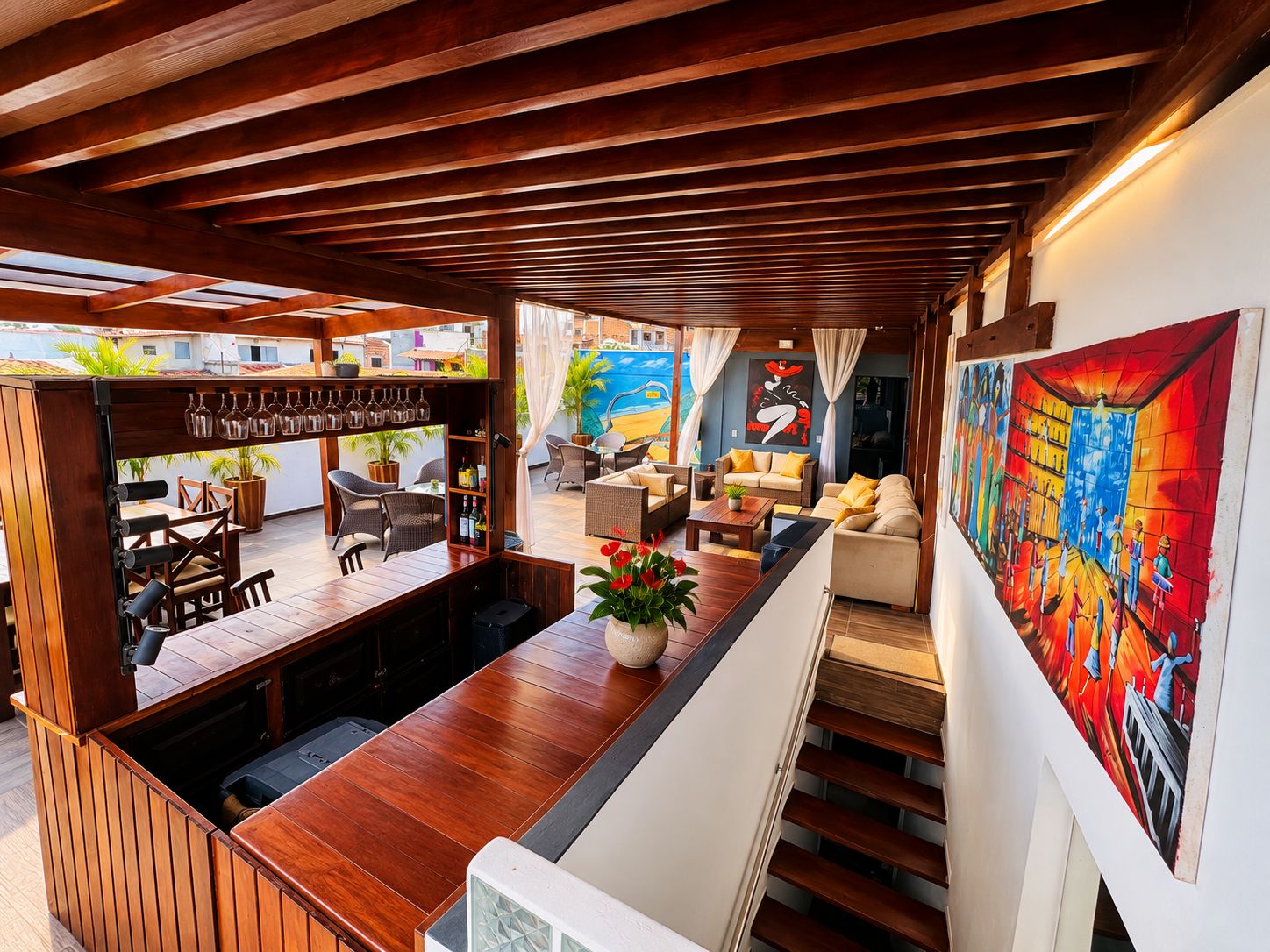 Área de bar com mobiliário de madeira, sala de estar com sofás e escada para um andar superior.