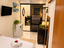 Quarto de hotel com cama, um pequeno frigorífico, televisão e obras de arte nas paredes.