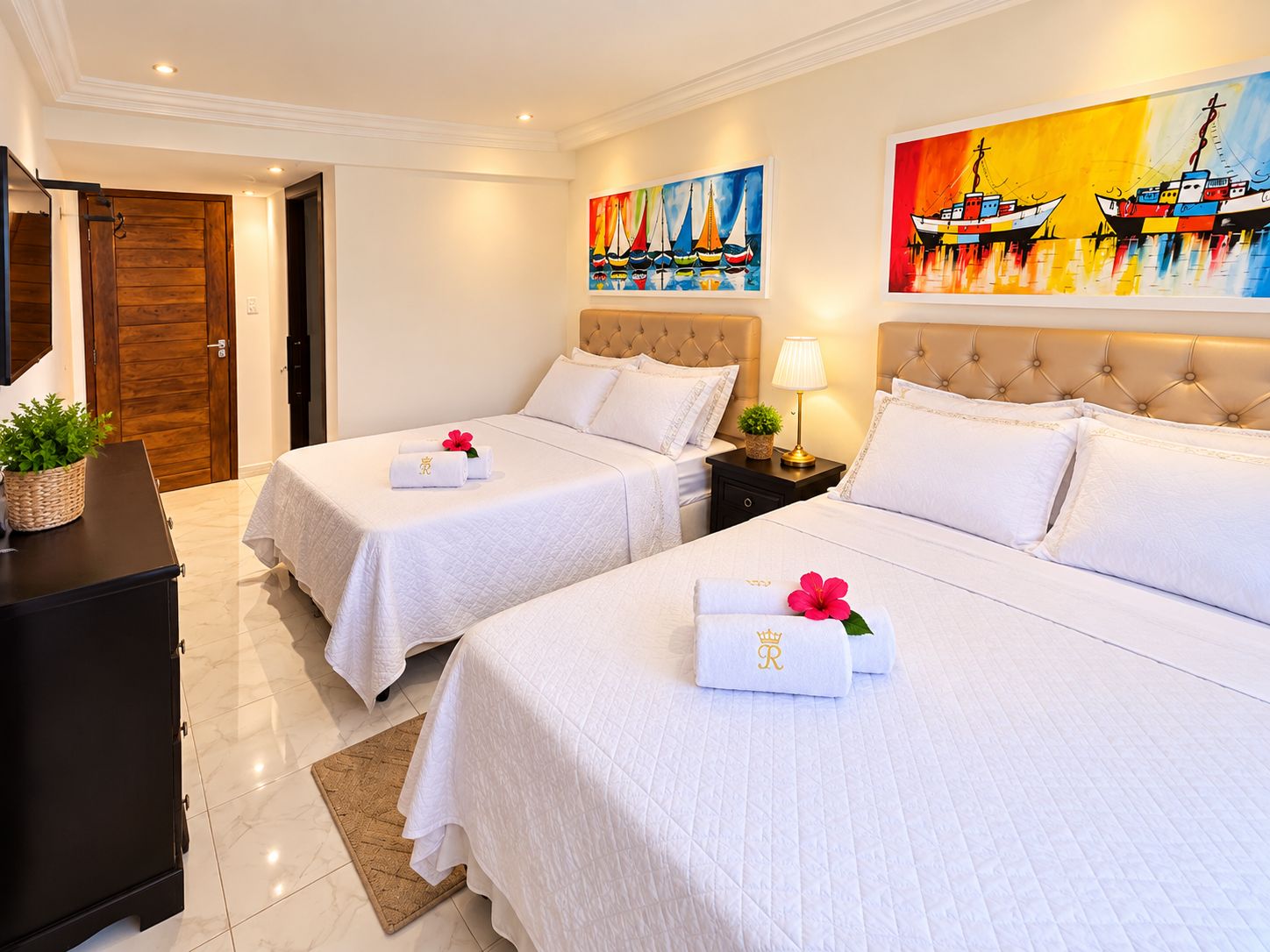 Quarto de hotel com duas camas, porta de madeira, uma mesinha com uma planta e obras de arte nas paredes.