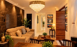 Uma sala de estar moderna com sofá, mesa de centro, cadeiras, lustre e quadros na parede.