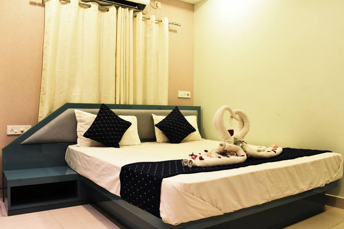 Cama bem arrumada com colcha branca e azul escura, duas almofadas e toalha decorativa em formato de cisne.