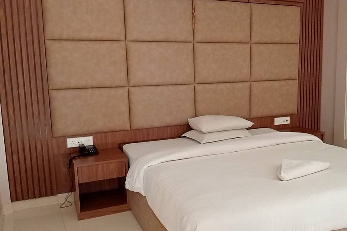 Cama bem arrumada com cabeceira acolchoada, mesa de cabeceira com telefone e janela com persianas.
