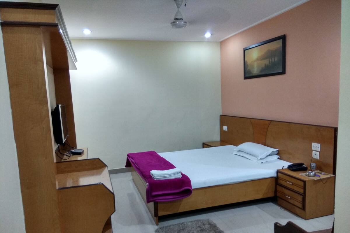 Um quarto bem arrumado com uma cama, mesas de cabeceira, uma escrivaninha e uma televisão.