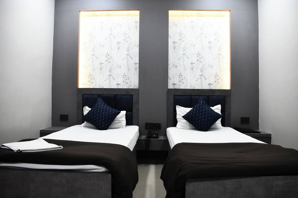 Quarto de hotel com duas camas, cada uma com cabeceira, mesa de cabeceira e janela com padrão floral.