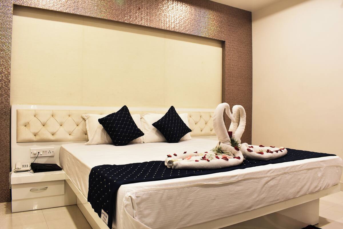 Uma cama bem arrumada com cabeceira branca, edredom com padrão preto e branco e almofadas decorativas.