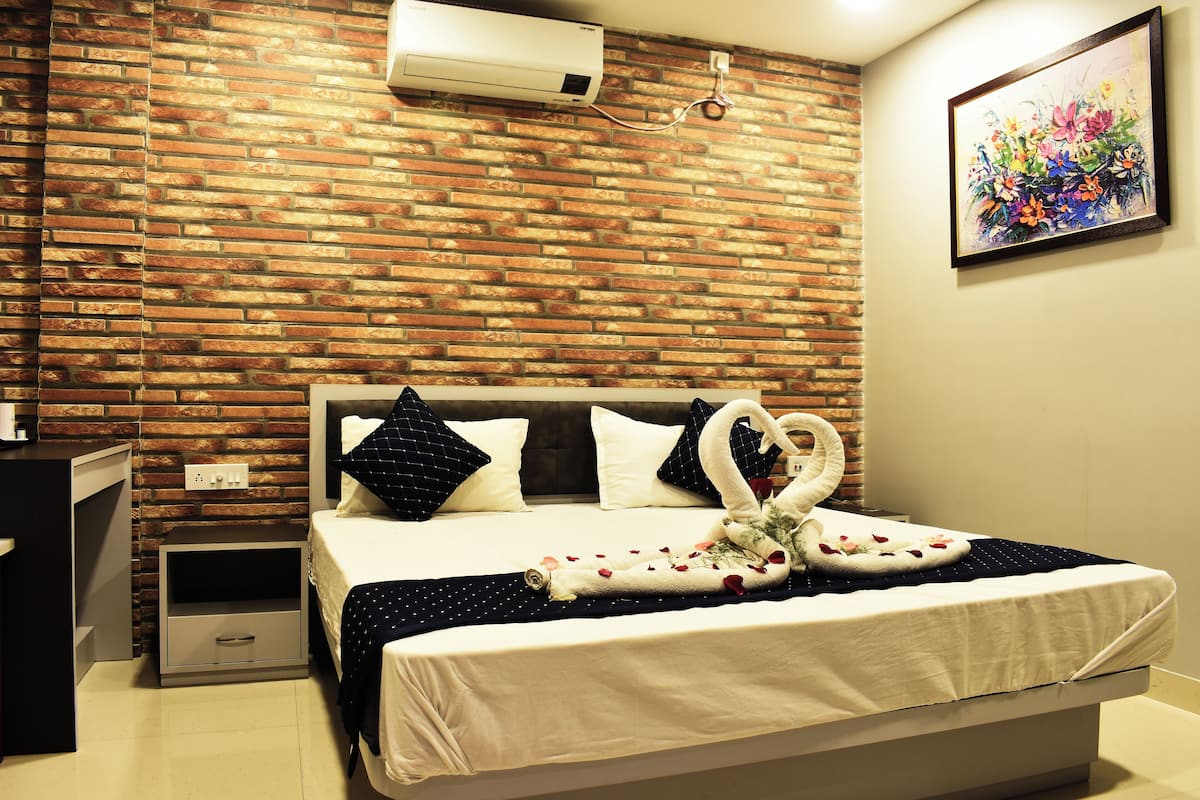 Quarto de hotel com parede em tijolos, cama com colcha branca, cisne decorativo feito de toalhas e um quadro na parede.
