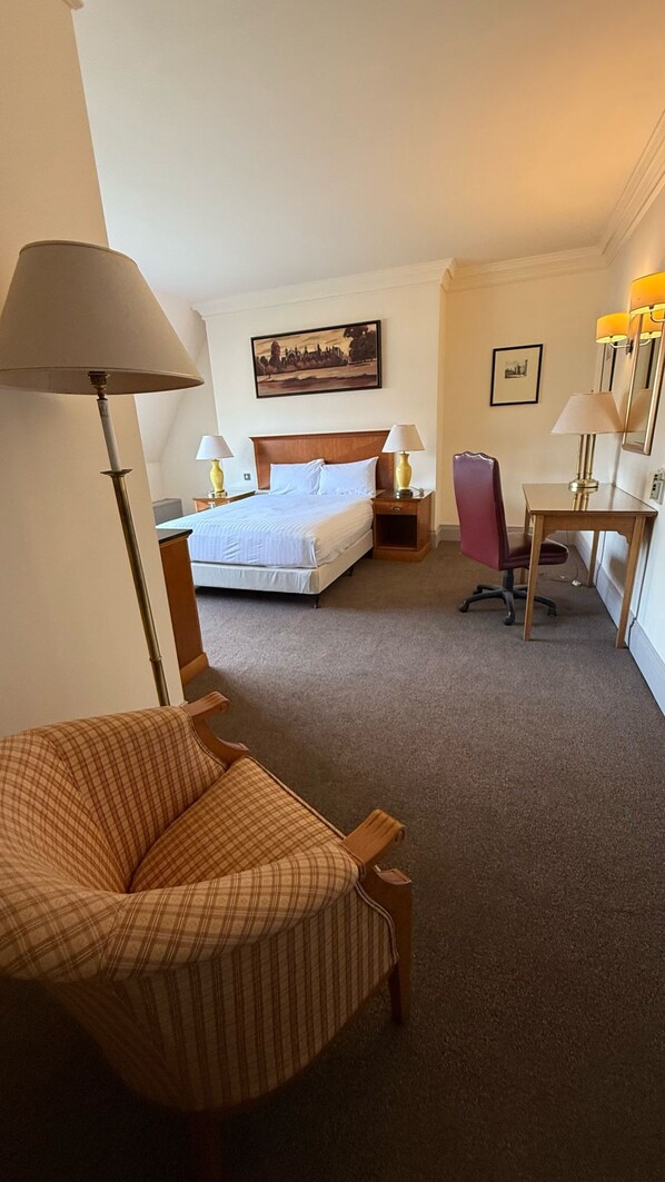 Quarto de hotel com cama, escrivaninha, cadeira e duas luminárias.