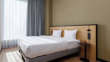 Quarto de hotel com uma cama grande, uma mesinha de cabeceira e vista para o exterior através de cortinas translúcidas.
