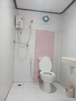 Uma casa de banho pequena e branca, com sanita, chuveiro e aquecedor fixado na parede.