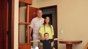 Quarto de hotel com uma cama, um guarda-roupa de madeira, um ventilador de teto e uma mesa pequena.