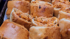 Uma variedade de produtos de panificação, incluindo pães e doces, dispostos em bandejas.