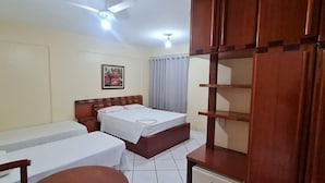 Quarto de hotel com cama, escrivaninha, cadeira, guarda-roupa e ventoinha no teto.