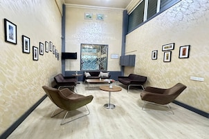 Um saguão de hotel moderno com uma área de estar central, quadros nas paredes e uma grande janela ao fundo.
