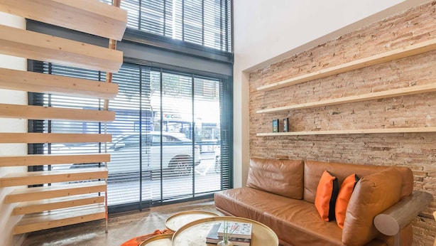 Uma sala de estar moderna com um sofá de couro marrom, assentos de madeira ripas e uma parede de tijolos em destaque.