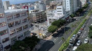 Rua urbana com prédios, carros estacionados e céu claro.