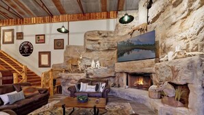 Um interior rústico com lareira de pedra, sofás de couro e escada de madeira.