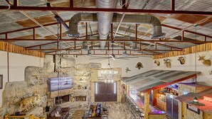 Um interior rústico com paredes de pedra, lareira, móveis de madeira e chifres de animais nas paredes.