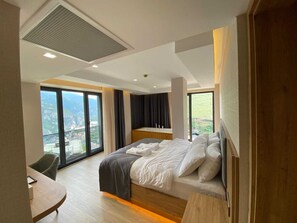 Quarto de hotel moderno com uma cama grande, uma mesa de trabalho e vista para uma paisagem montanhosa.