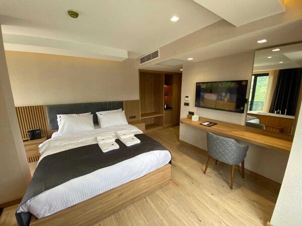 Quarto de hotel moderno com uma cama grande, uma escrivaninha e uma televisão.