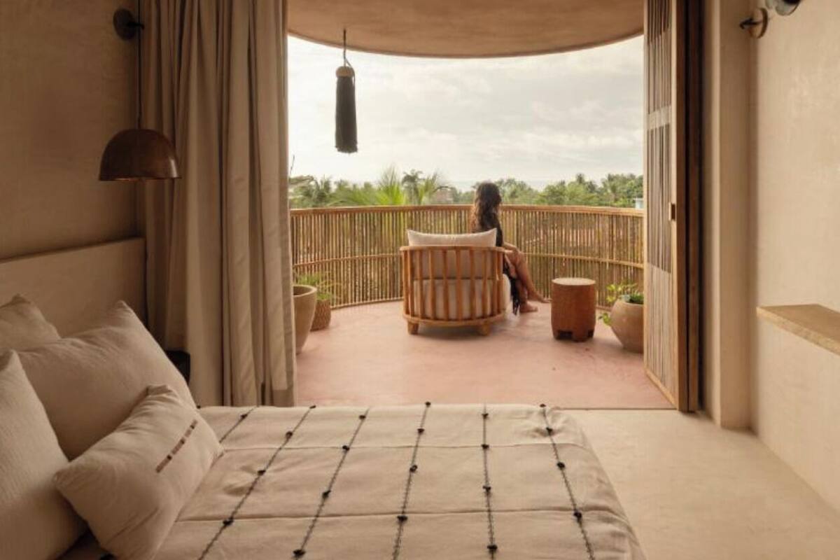 Quarto com cama, cadeira e varanda com vista para área verde.