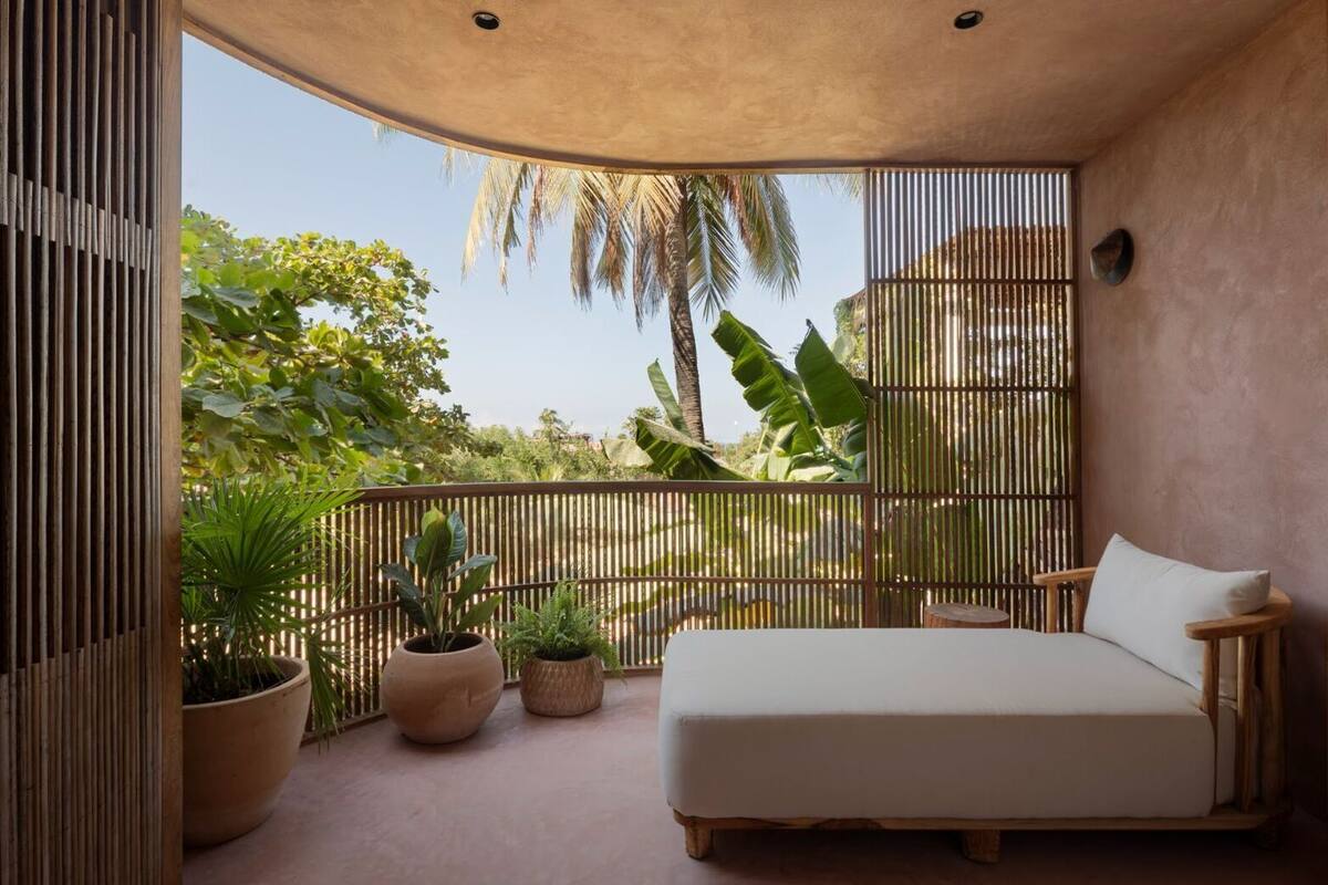 Quarto com teto curvo, cama, mesa pequena e plantas em vasos.