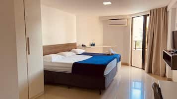 Quarto de hotel com cama, escrivaninha, cadeira, televisão e banheiro.