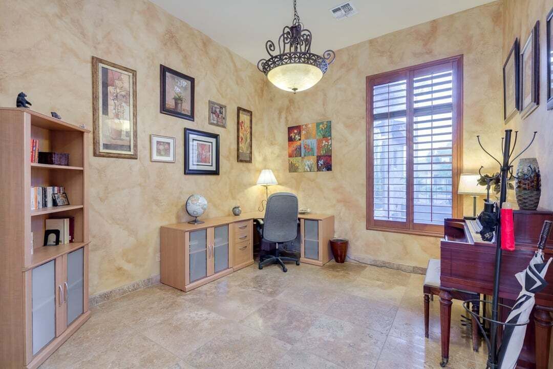 Quarto com escrivaninha, cadeira, estante e uma janela grande com persianas.
