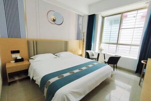 Quarto de hotel com cama, mesa de cabeceira, cadeira e janela com cortinas.