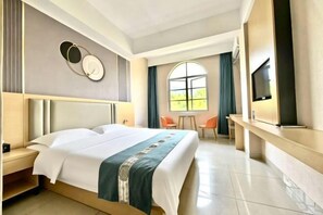 Quarto de hotel com cama, escrivaninha, cadeira, televisão e janela.