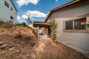 Um imóvel residencial com um vestíbulo coberto, um caminho de terra e um pequeno jardim com uma planta florida vermelha.