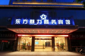 Entrada de hotel com placa em caracteres chineses, área de acesso coberta e plantas em vasos.