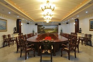 Uma sala de reuniões formal com uma grande mesa oval, cadeiras de madeira, um candelabro e quadros nas paredes.