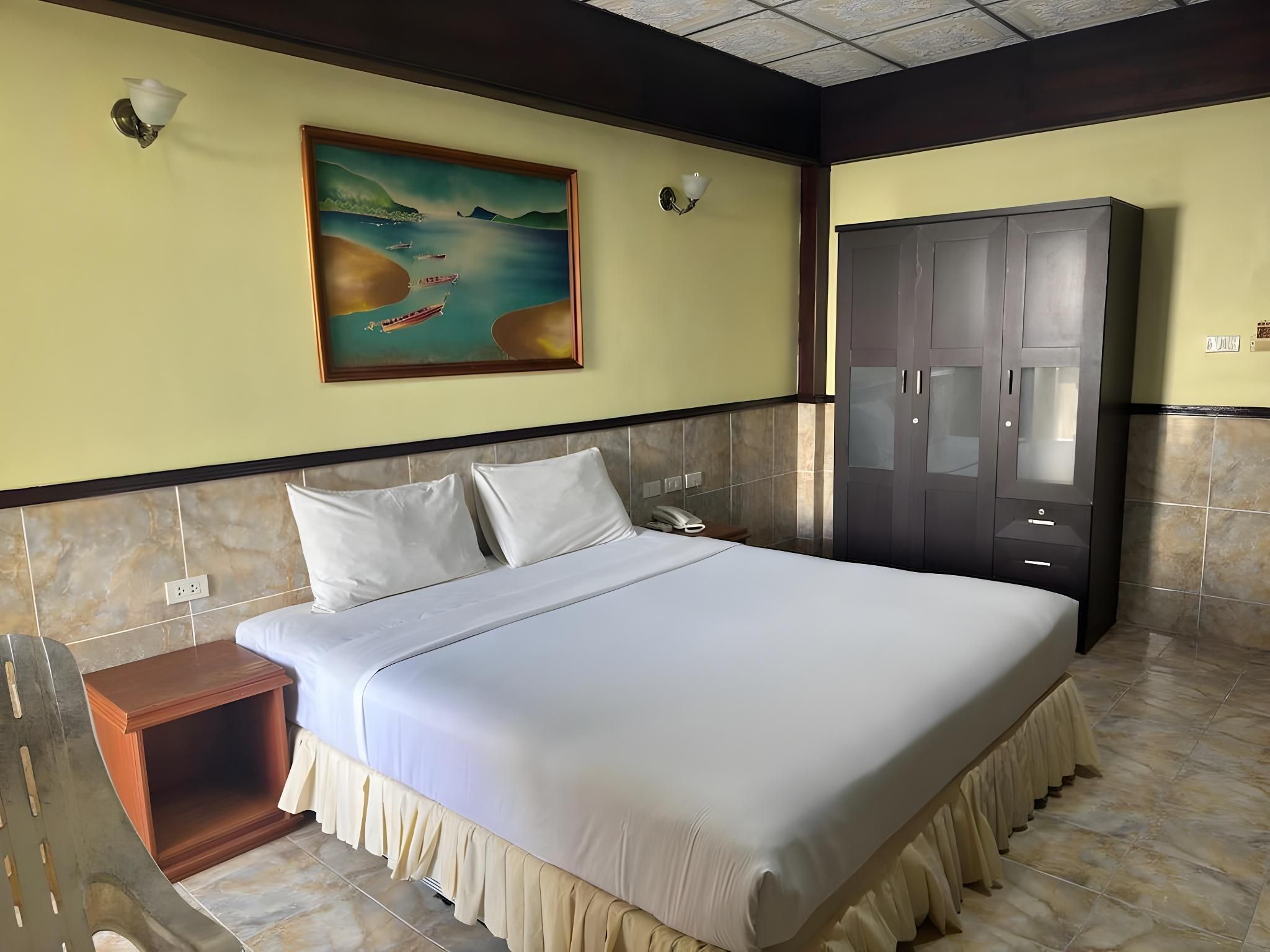 Quarto de hotel com cama, mesa de cabeceira, guarda-roupa e uma pintura de uma cena de praia.