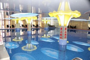 Uma área de piscina com água azul cristalina, estruturas flutuantes amarelas e azuis, e piso revestido de azulejos.