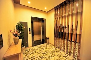 Um elevador com design moderno, piso estampado e uma planta em vaso sobre uma mesa.