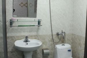 Casa de banho com lavatório com coluna, sanita e prateleira de vidro sobre o lavatório, e zona de duche.
