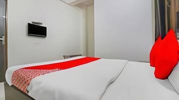 Quarto de hotel com uma cama, televisão na parede e um travesseiro vermelho.