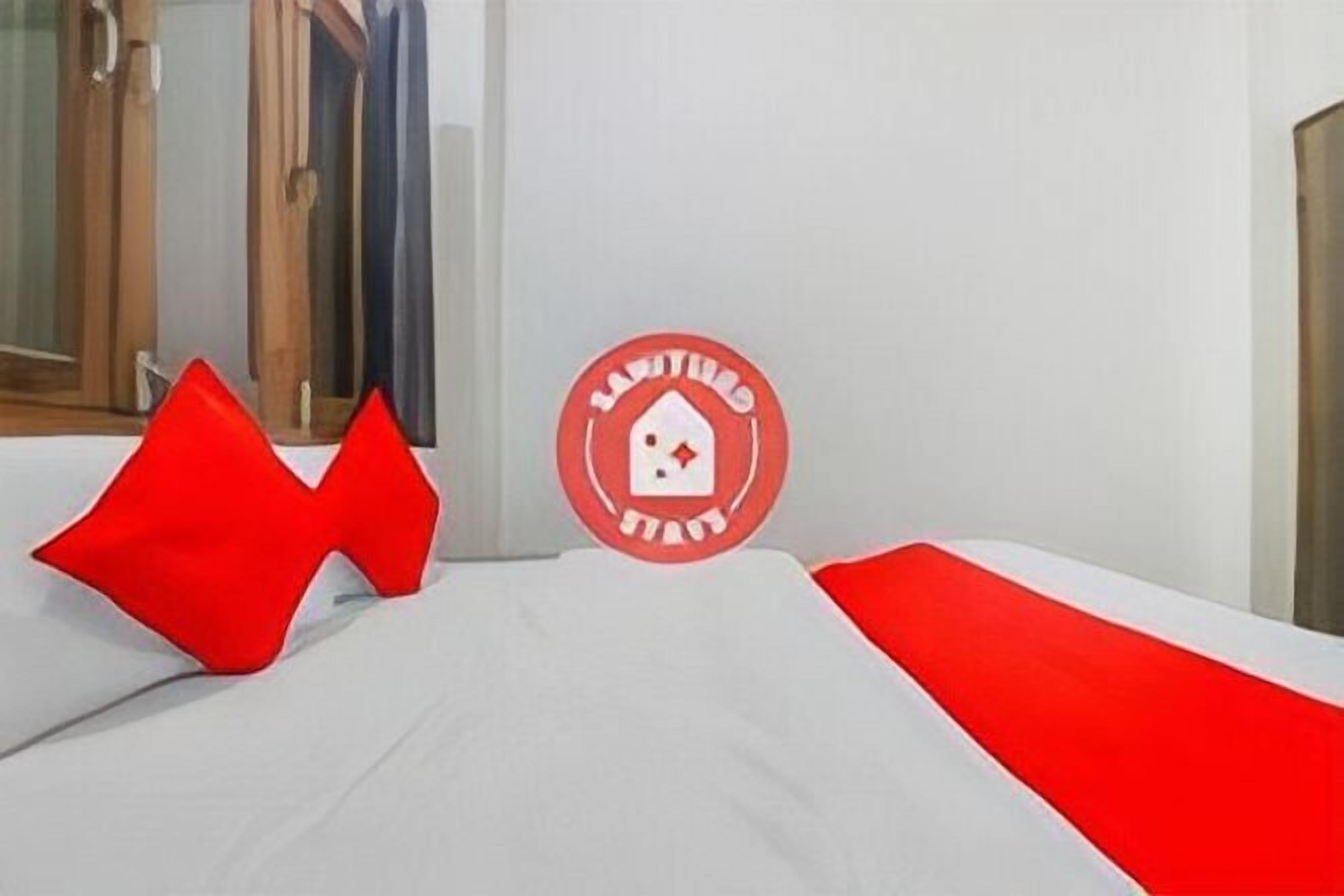 Quarto de hotel com uma cama, um travesseiro vermelho e um logotipo circular na parede.