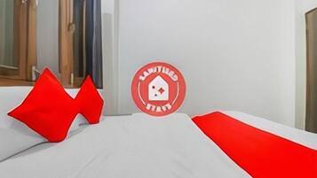 Quarto de hotel com uma cama, um travesseiro vermelho e um logotipo circular na parede.