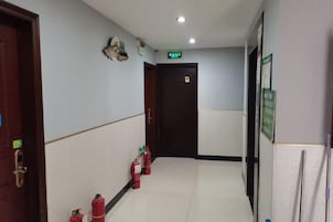 Corredor com portas, um extintor de incêndio e uma placa de saída verde.